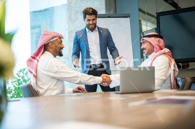 Two Saudi Arabian Gulf businessmen shake hands in the meeting room ...