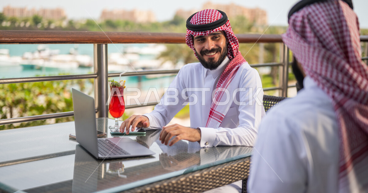 Saudi Arab Gulf co-workers gathered in a café in a Gulf hotel, using a ...