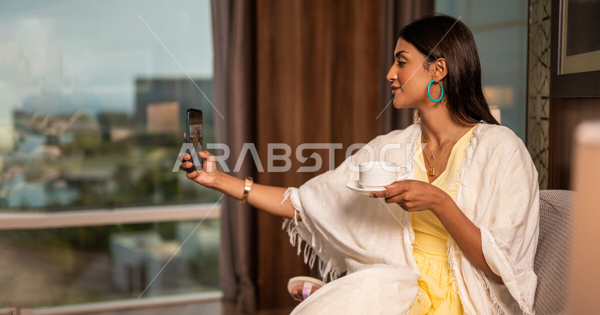 امرأة عربية خليجية سعودية ترتدي زي صيفي، الاستمتاع بالعطلة داخل المنزل، التقاط صورة تذكارية من ...