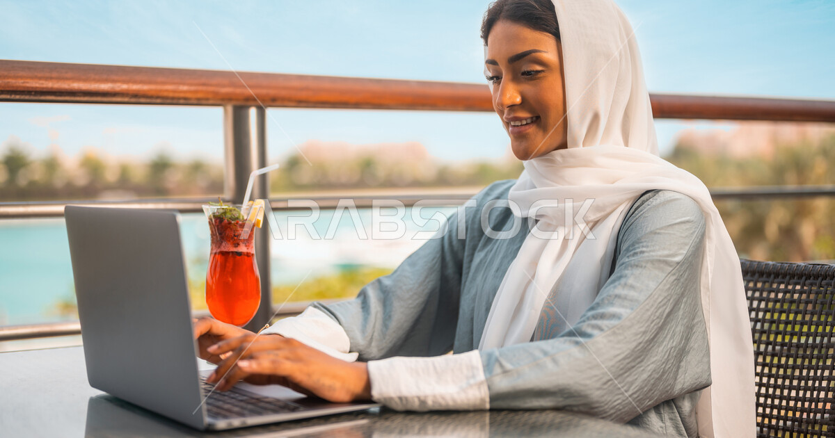 A Saudi Arabian Gulf business woman sitting in front of a laptop in a ...