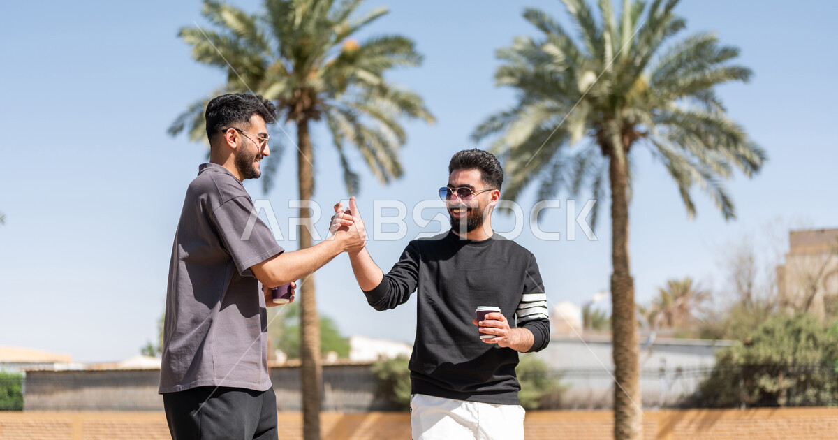 Two young Saudi Arabs from the Gulf meet in a public park and shake ...