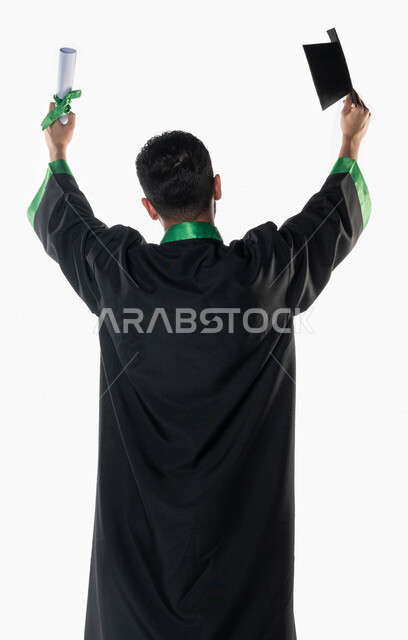 Portrait from the back of a Saudi Arabian Gulf student wearing a graduation gown, raising the ...