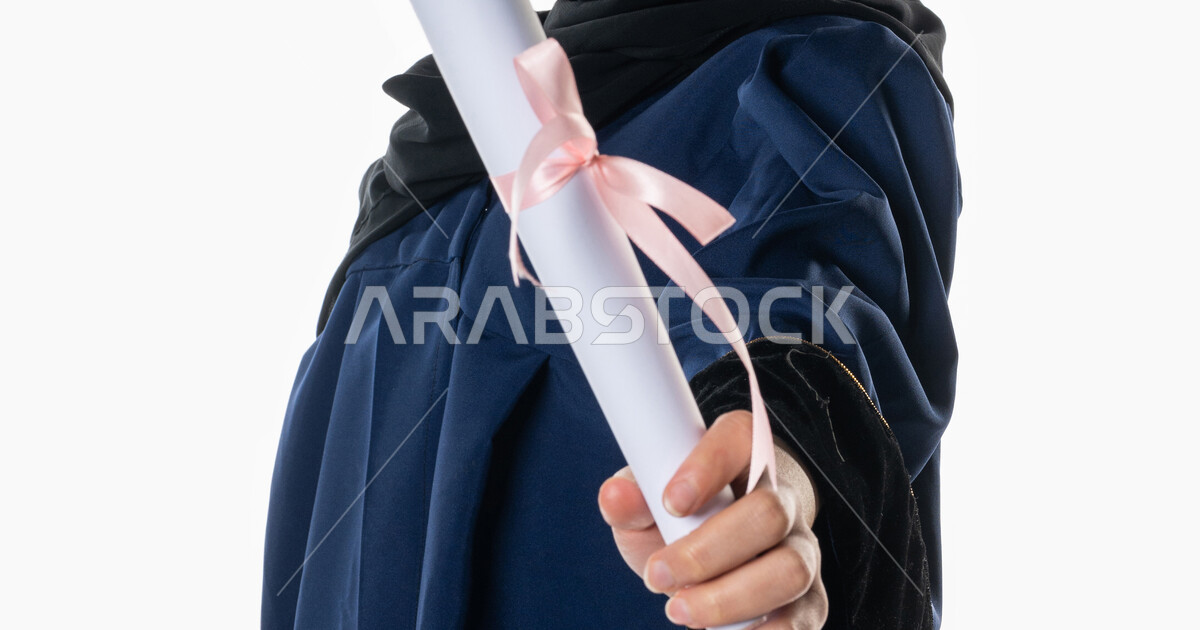 Portrait of a Saudi Arabian Gulf student wearing an abaya and graduation cap, holding a ...