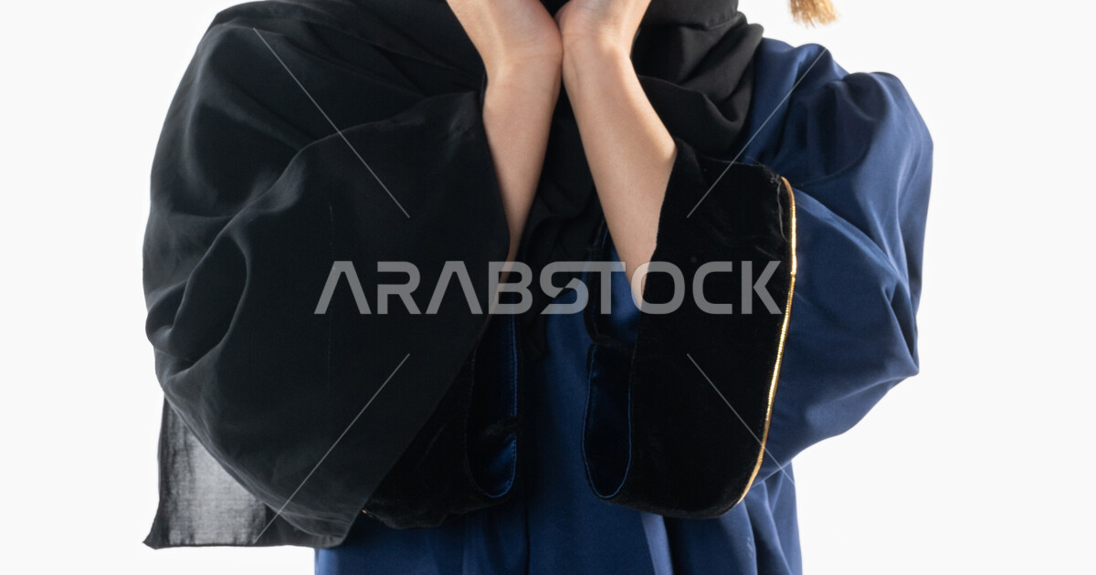Portrait of a Saudi Arabian Gulf student wearing an abaya and graduation cap, putting her hands ...