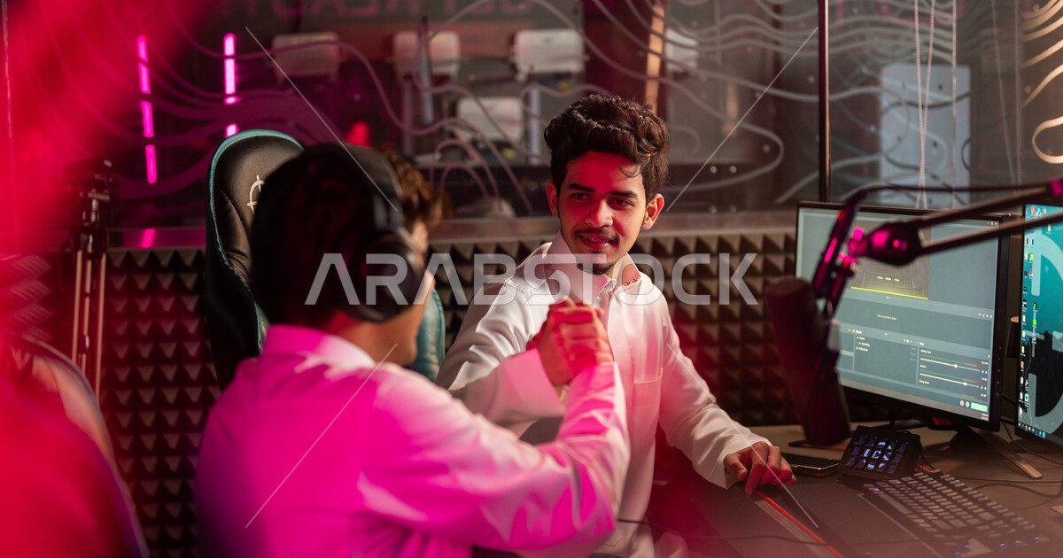 Two young Saudi Arabian Gulf teenagers shaking hands in an electronic ...