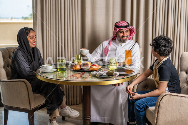 A Saudi Arabian Gulf family sitting in the restaurant, a dining table ...
