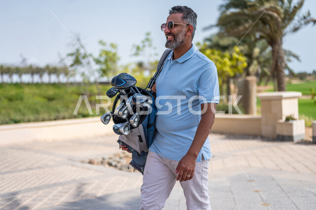 A Saudi Arabian Gulf man wearing a sports uniform, carrying a golf bag ...