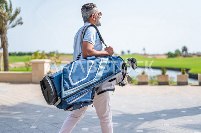 A Saudi Arabian Gulf man wearing a sports uniform, carrying a golf bag ...