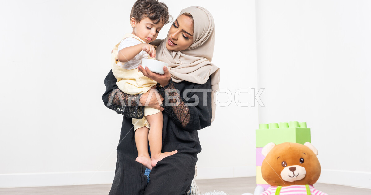 A veiled Saudi Gulf Arab mother carrying her young child, a mother ...