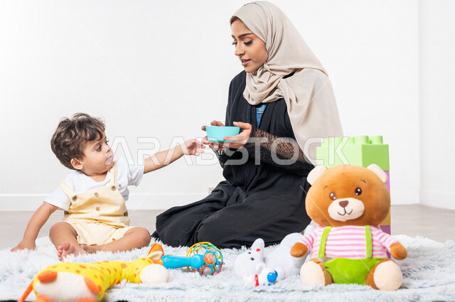 A veiled Saudi Gulf Arab mother holds a plate of children's food and ...