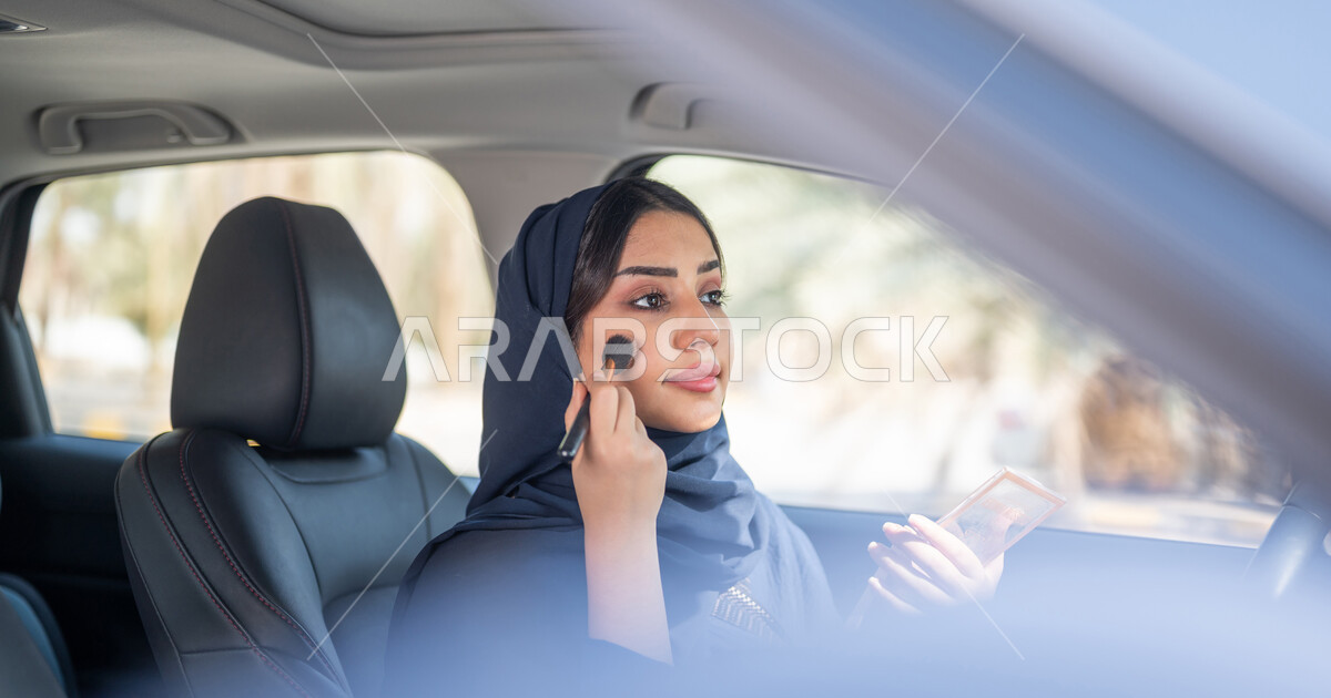 A veiled Saudi Arabian Gulf woman sitting in the car and decorating her ...
