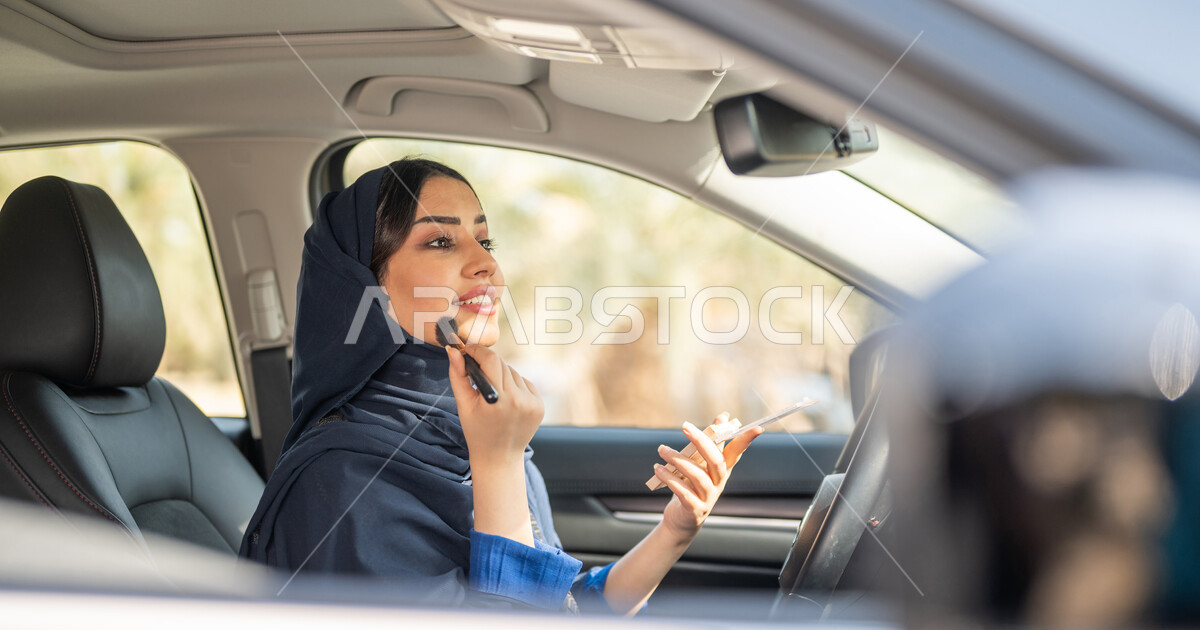A veiled Saudi Arabian Gulf woman sitting in the car and decorating her ...