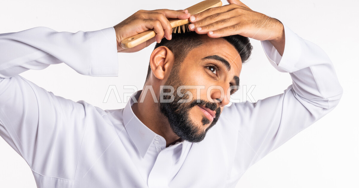 A close-up portrait of a Saudi Arabian Gulf man, styling his hair with ...