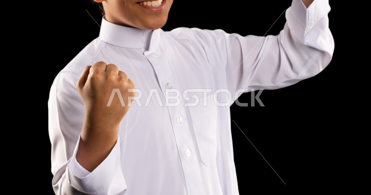 Portrait of a Saudi Arabian Gulf boy wearing a Saudi dress raising his ...
