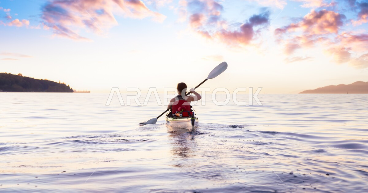 Back view of a young man riding a rowing boat, doing water sports ...