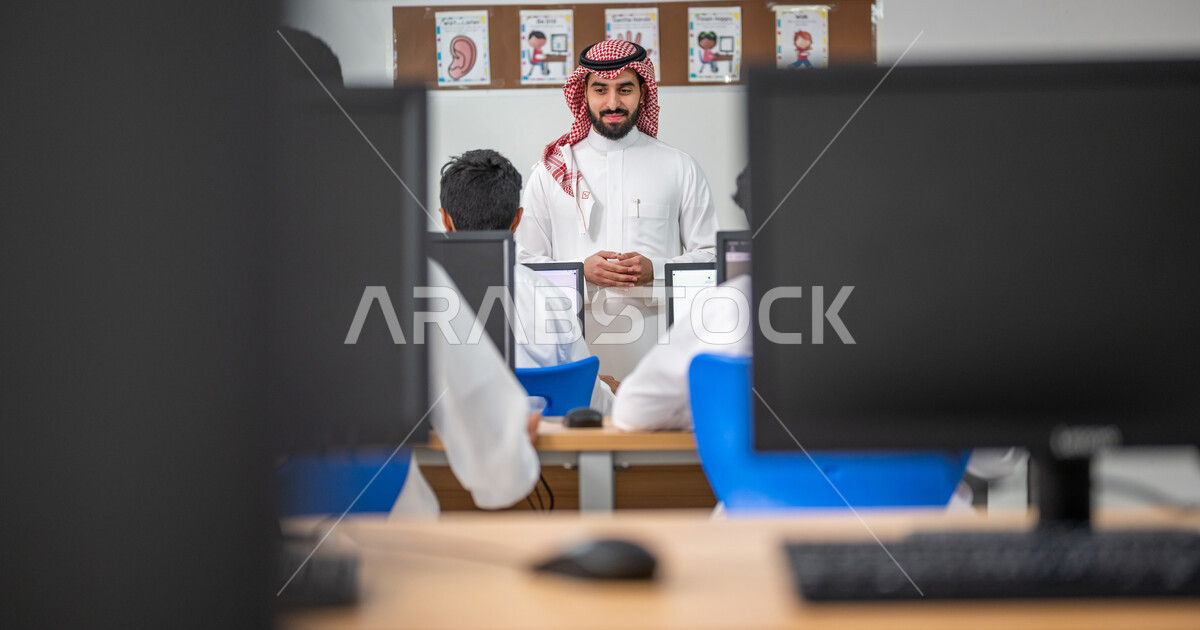 صورة مقربة لشاشات الكمبيوتر، معلم عربي خليجي سعودي في معمل الحاسب الآلي