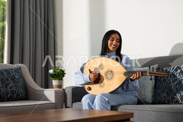 A Saudi Arabian Gulf woman sitting at home, playing the oud instrument ...