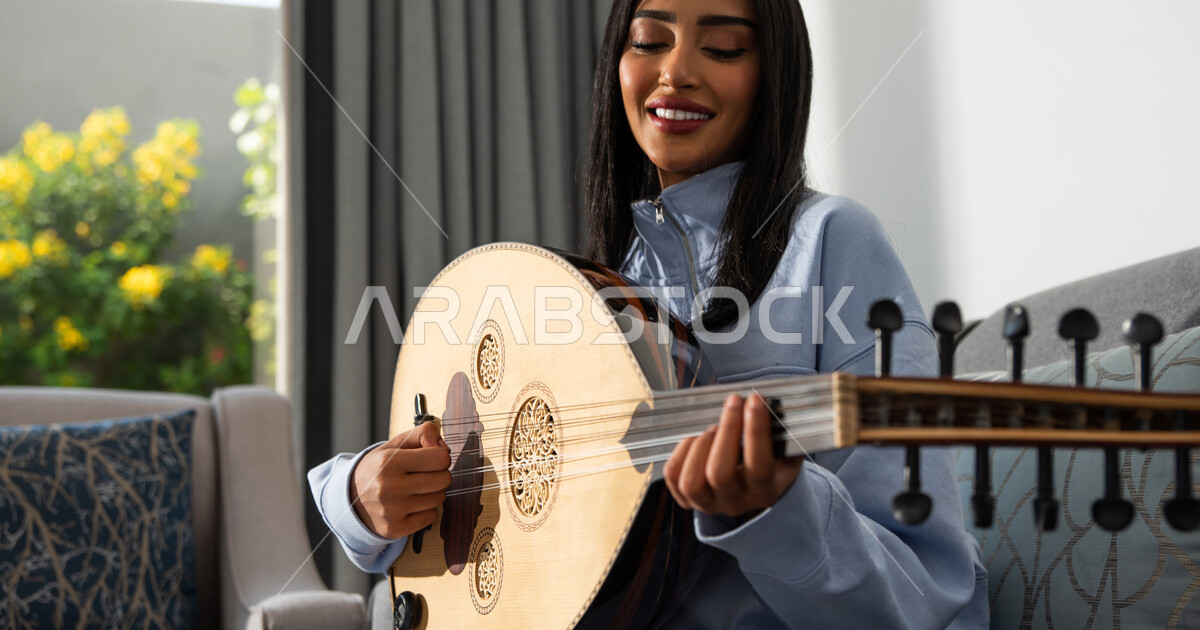 A Saudi Arabian Gulf woman sitting at home, playing the oud instrument ...