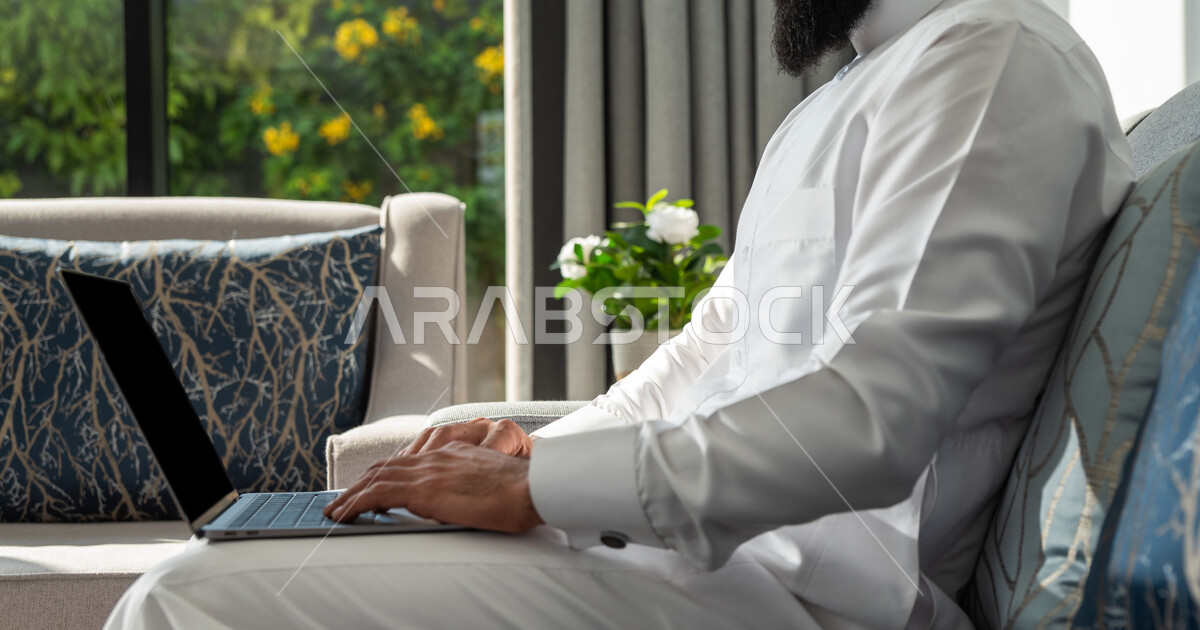 A Saudi Arabian Gulf man sitting at home, using a laptop, browsing the ...