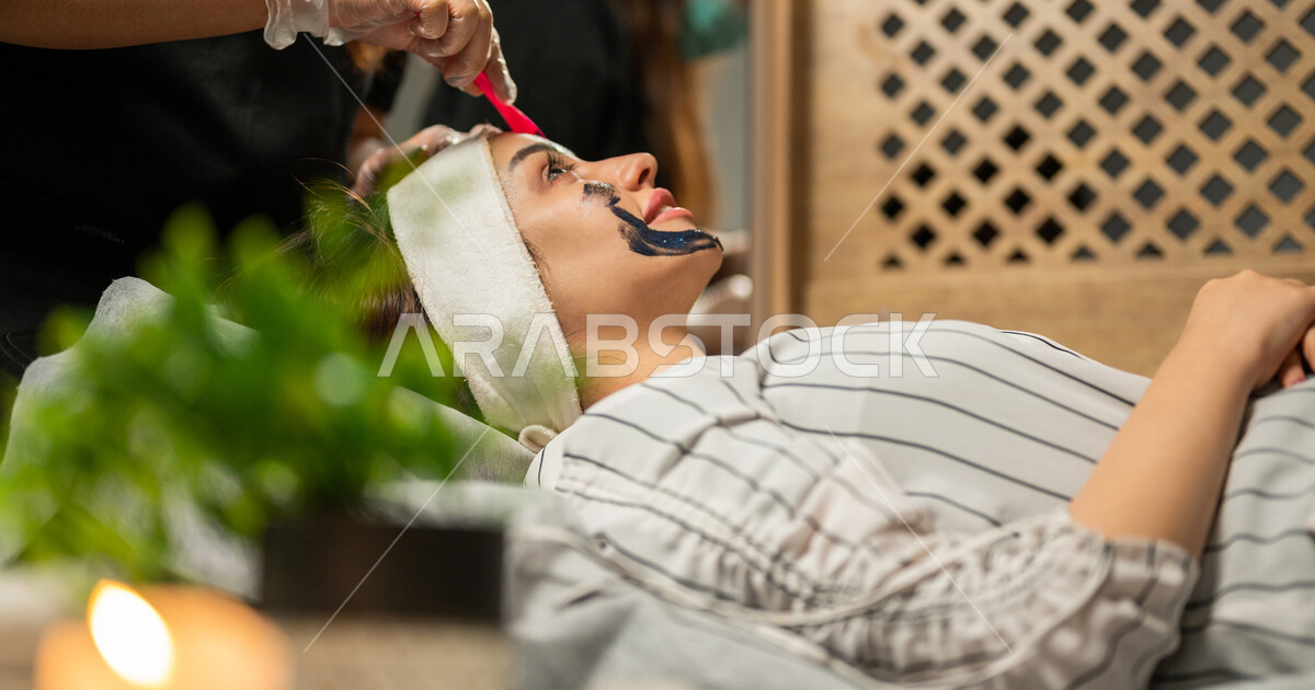 A Saudi Arabian Gulf woman in a women’s beauty salon, putting a mud ...