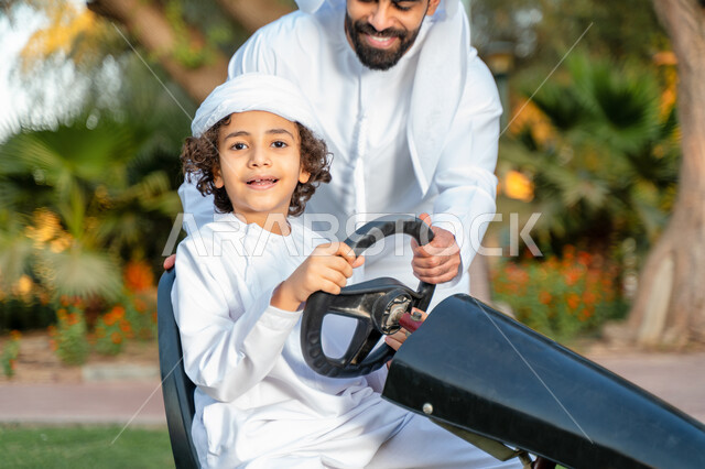 Arab Gulf Emirati father wearing traditional costume playing with his ...