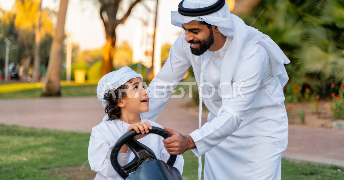 Arab Gulf Emirati father wearing traditional costume playing with his ...
