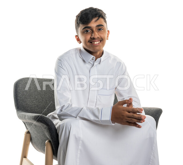 Portrait of a smiling Saudi Arabian Gulf boy, sitting on a chair ...