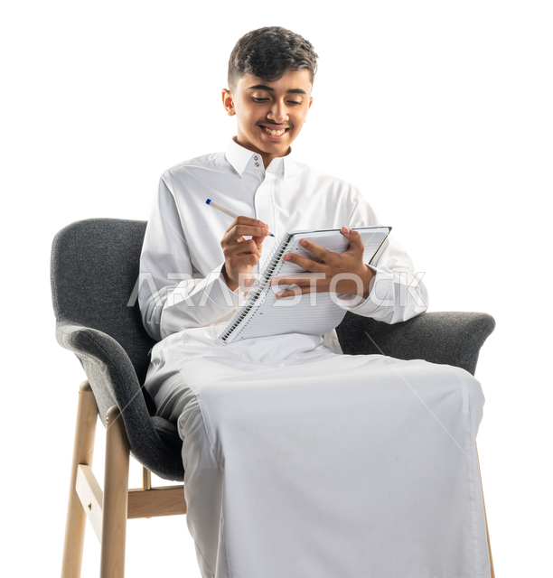 Portrait of a Saudi Arabian Gulf boy, sitting on a chair, doing ...