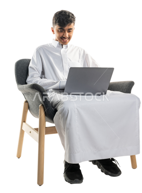Portrait of a Saudi Arabian Gulf boy, sitting on a chair, using a ...