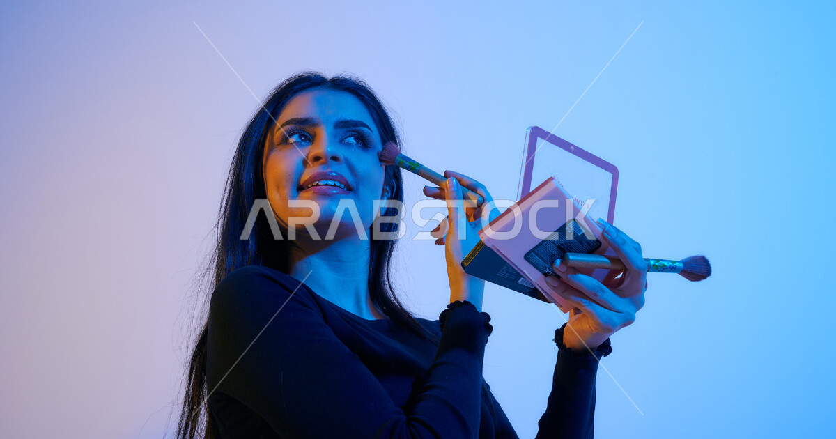 بورتريه لإمرأة عربية خليجية سعودية تحمل بيدها أدوات تجميل، خلفية ملونة ...