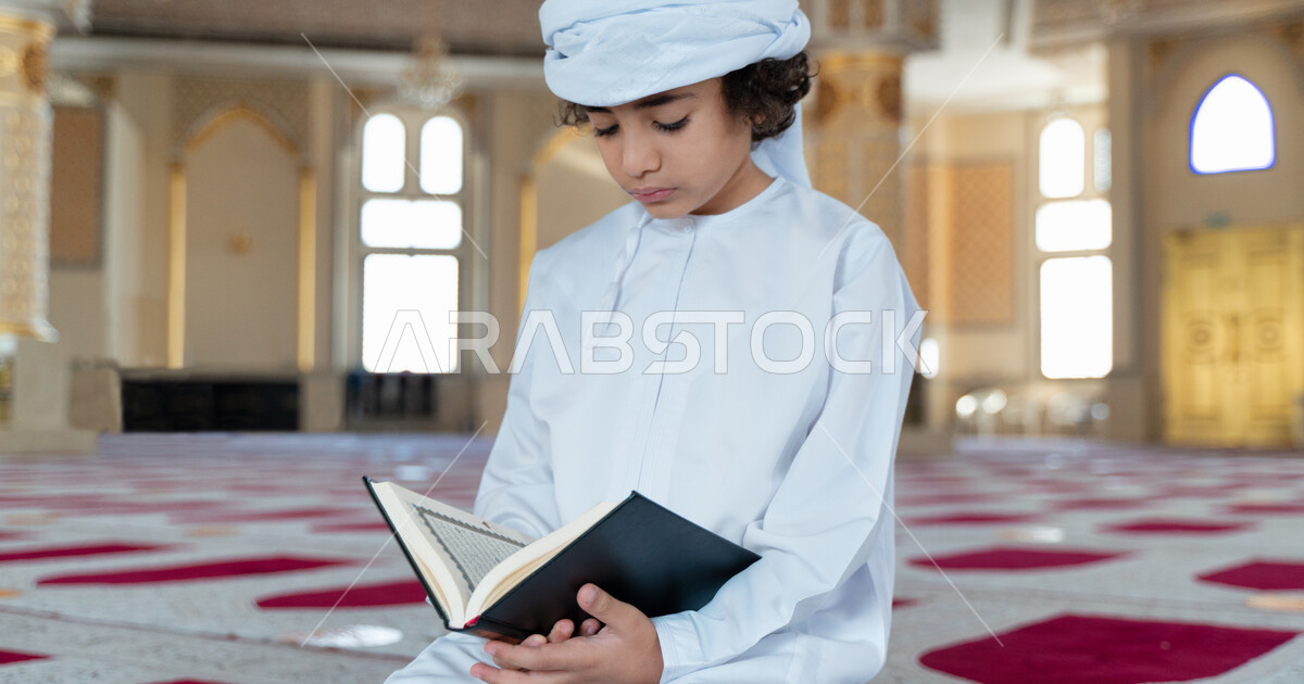 ولد صغير عربي خليجي إماراتي في أحد المساجد العربية، يحمل بيده المصحف ...