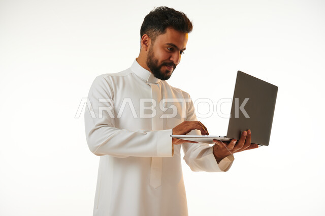 Portrait of a Saudi Arab Gulf man holding a laptop in his hand, working ...