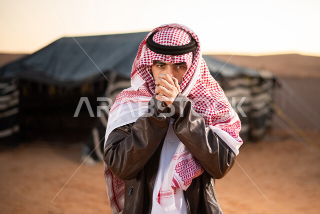 A Saudi Arabian Gulf man wearing warm winter clothes and blowing with ...