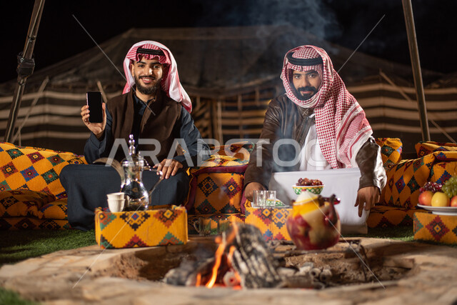 Two Saudi Arabian Gulf men wearing a warm winter jacket, a mobile phone ...