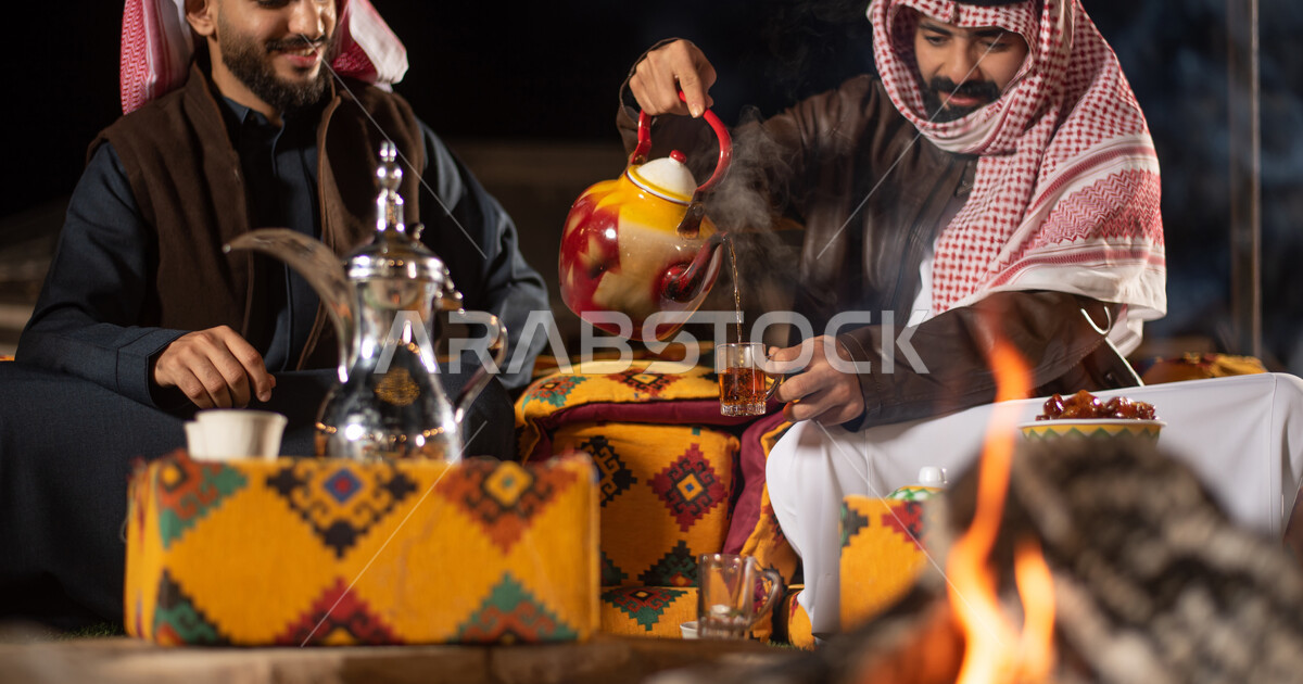 Two Saudi Arab Gulf men dressed in warm winter clothes, serving hot tea ...