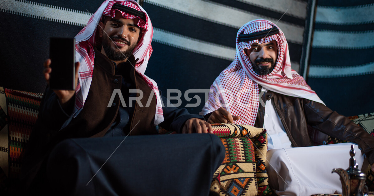 Two Saudi Arab Gulf men wearing warm winter clothes, a mobile phone ...