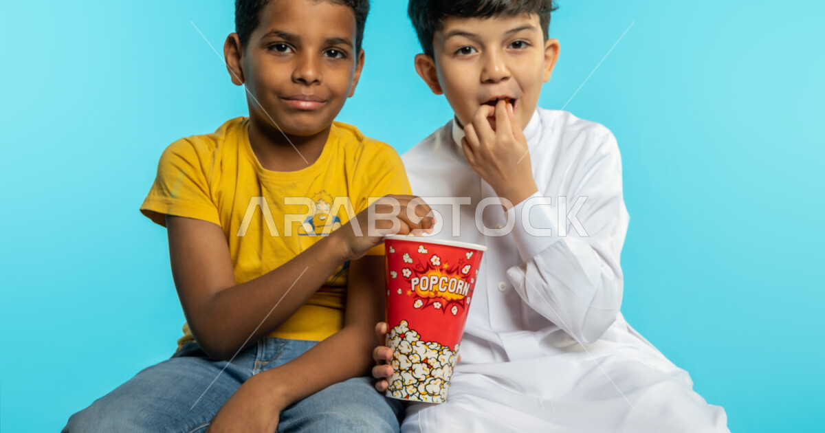 Portrait of two Saudi Arabian Gulf children enjoying eating popcorn ...