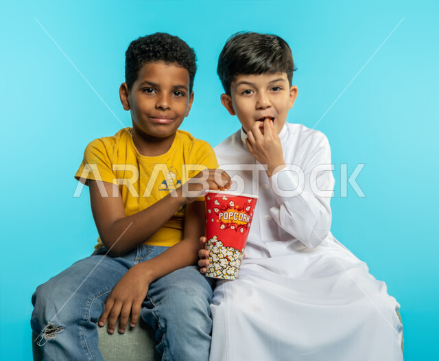 Portrait of two Saudi Arabian Gulf children enjoying eating popcorn ...