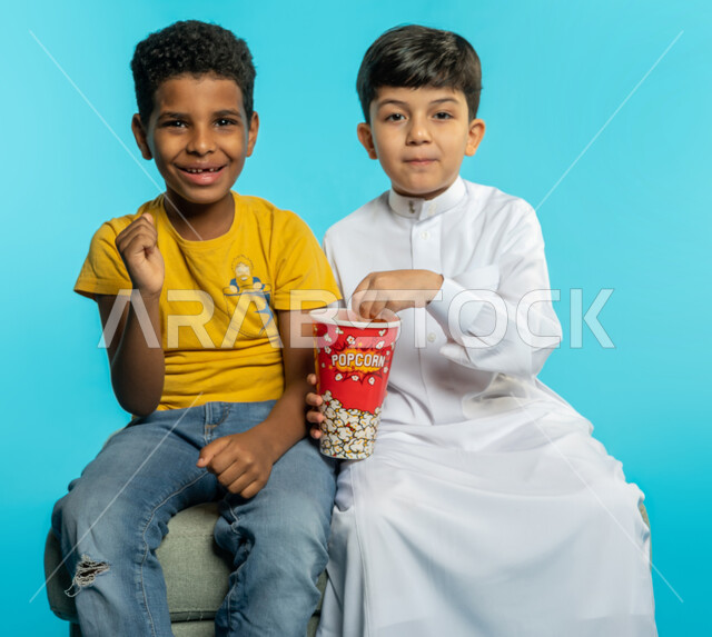 Portrait of two Saudi Arabian Gulf children enjoying eating popcorn ...
