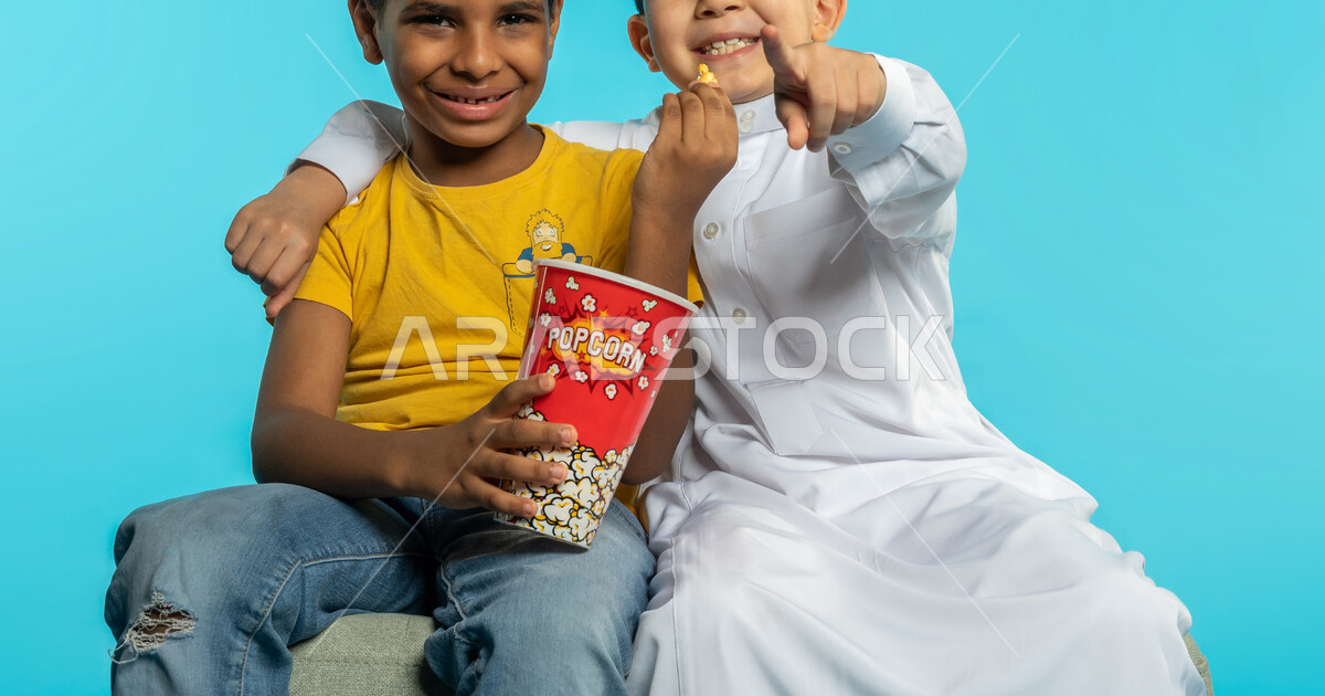 Portrait of two Saudi Arabian Gulf children enjoying eating popcorn ...
