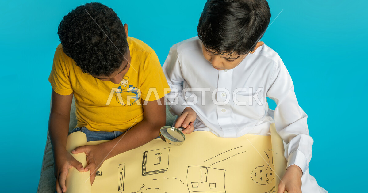 Portrait of two Saudi Arabian Gulf children using a magnifying glass ...