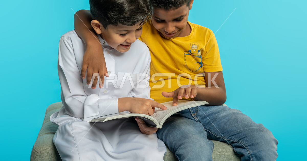 Portrait of two Saudi Arabian Gulf children reading books, enjoying ...