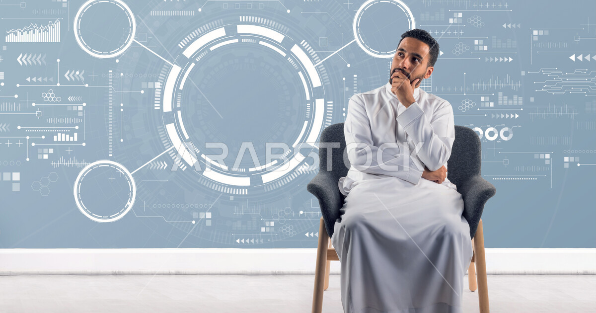 A Saudi Gulf Arab man sits on a chair and puts his hand on his chin ...