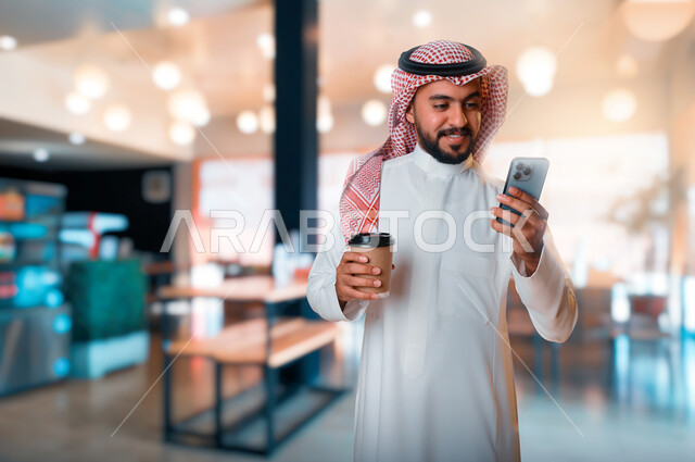 A Saudi Arabian Gulf youth using a mobile phone with a cup in his hand ...