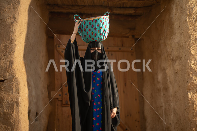 A Saudi Gulf Arab woman wearing a burqa, carrying a straw basket on her ...