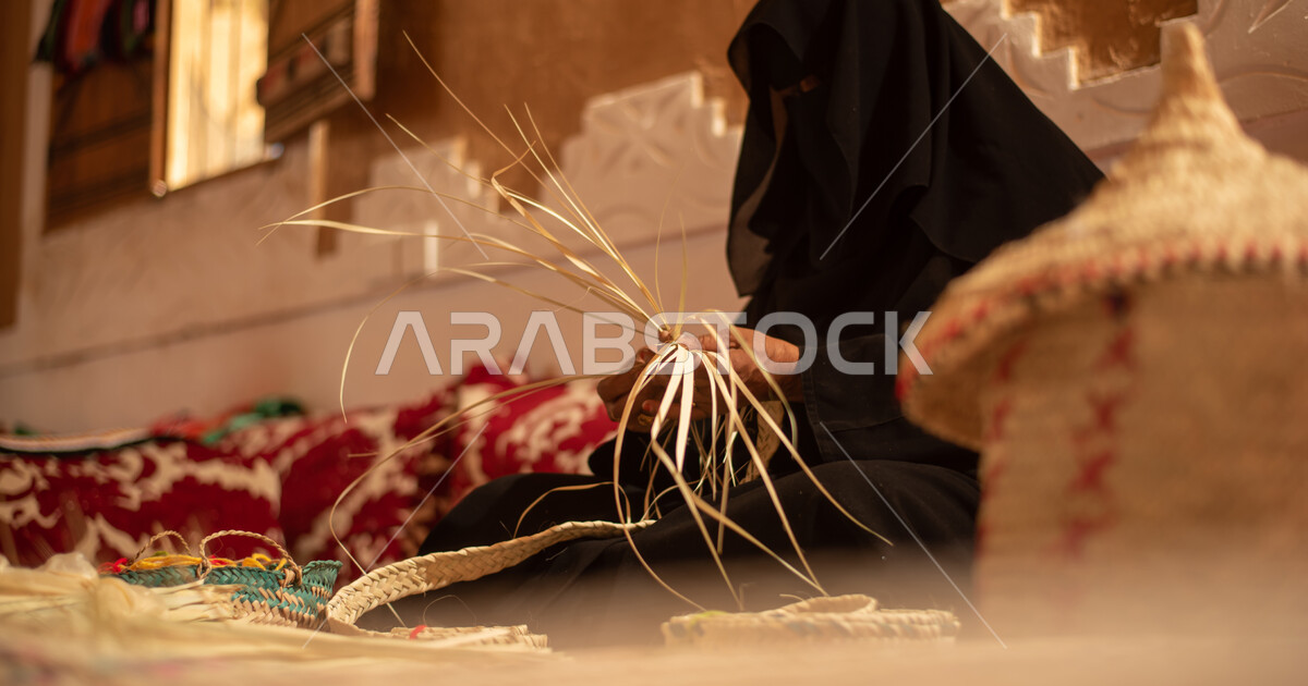 A Saudi Arab Gulf woman wearing a veil braids wicker palms, traditional ...