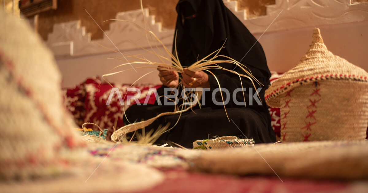 A Saudi Arab Gulf woman wearing a veil braids wicker palms, traditional ...