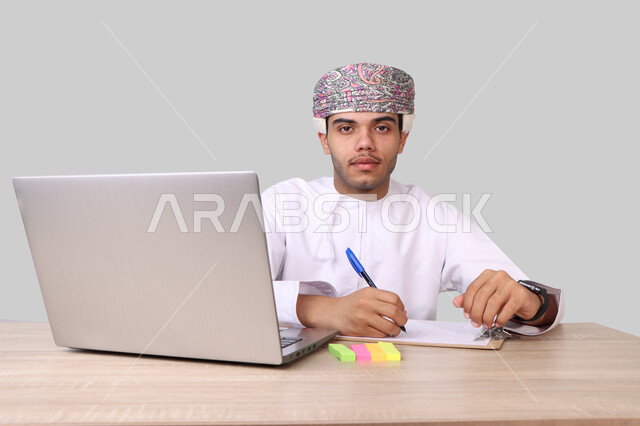 An Arab Omani Gulf man in traditional dress, holding a pen in his hand ...