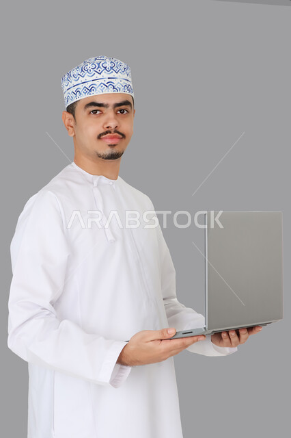 Portrait of an Arab Gulf Omani man holding a laptop in his hand ...