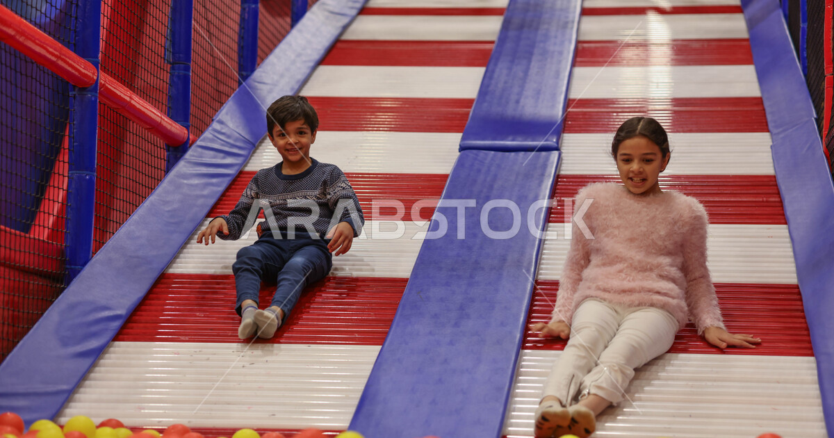 Two Saudi Arabian Gulf children enjoying playing on a skating game ...